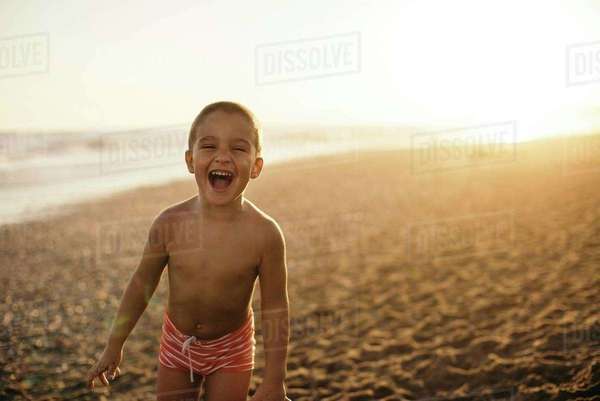 Happy shirtless boy smiling and looking at camera while standing on ...
