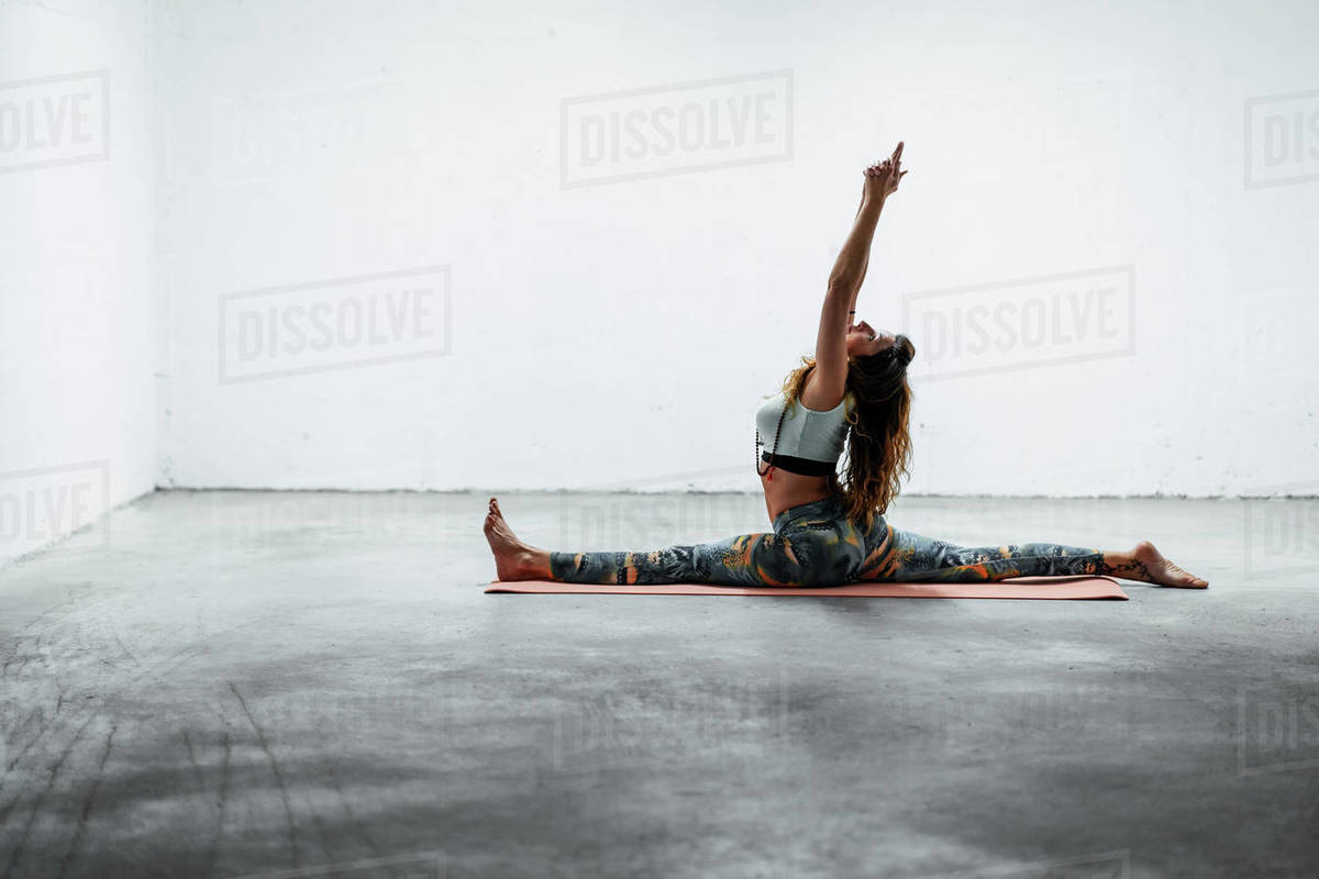 Side view of young flexible female in sportswear doing front split with ...