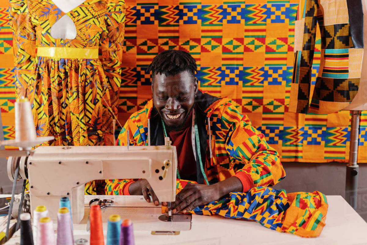 Happy black male tailor creating national costume of colored fabric ...