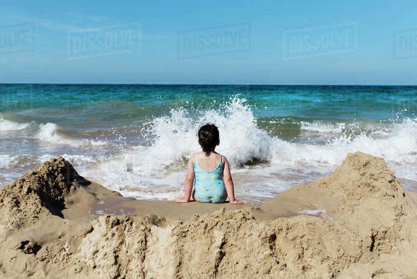 Back view of unrecognizable little girl in swimsuit sitting on sandy ...