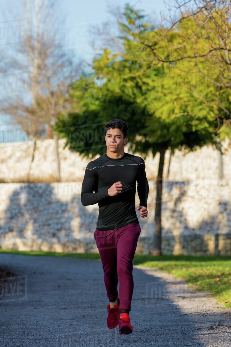 Full length ethnic male athlete running on path during fitness workout ...