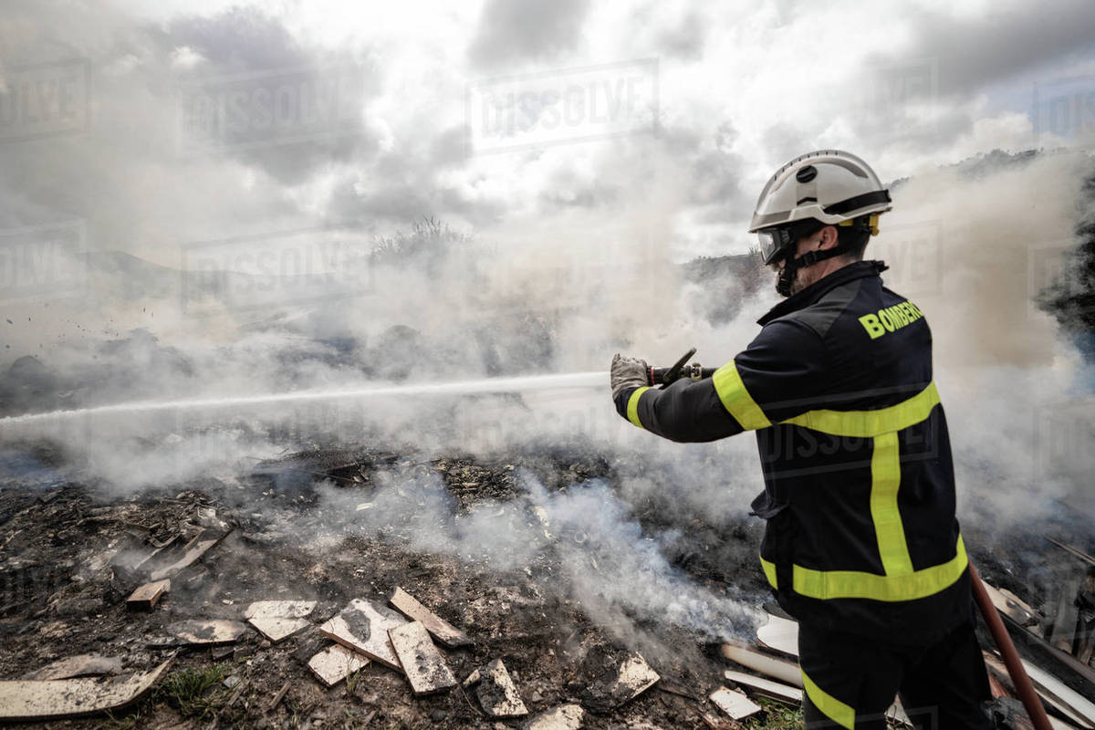 Side view of brave fireman in protective uniform standing with hose and ...