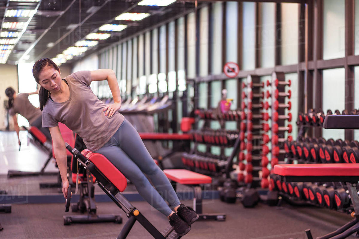 Strong young Asian sportswoman in active wear doing side bends with ...