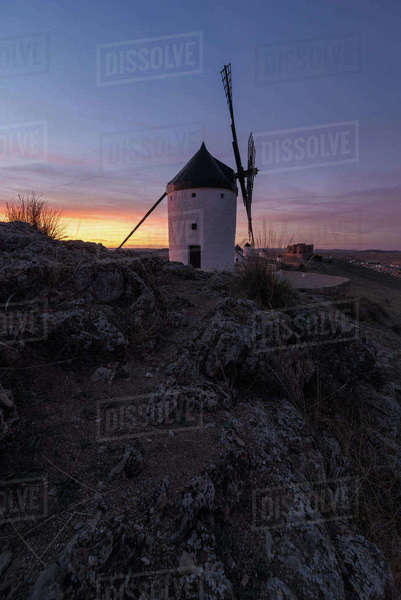 Aged windmill located on rocky cliff near medieval castle against ...