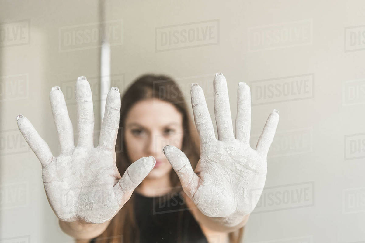 Attractive woman showing palms in chalk powder near pole and white wall ...