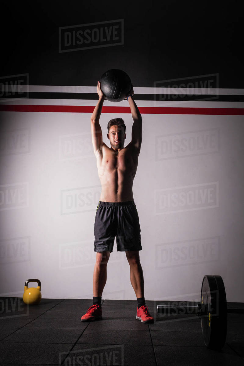 athletic young shirtless guy jumping and tossing big ball on wall in ...