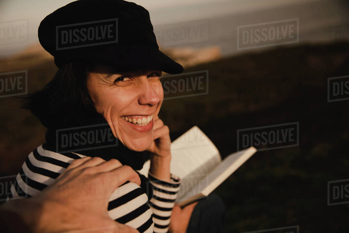 Back view of cheerful elegant lady in cap holding volume with crop hand ...