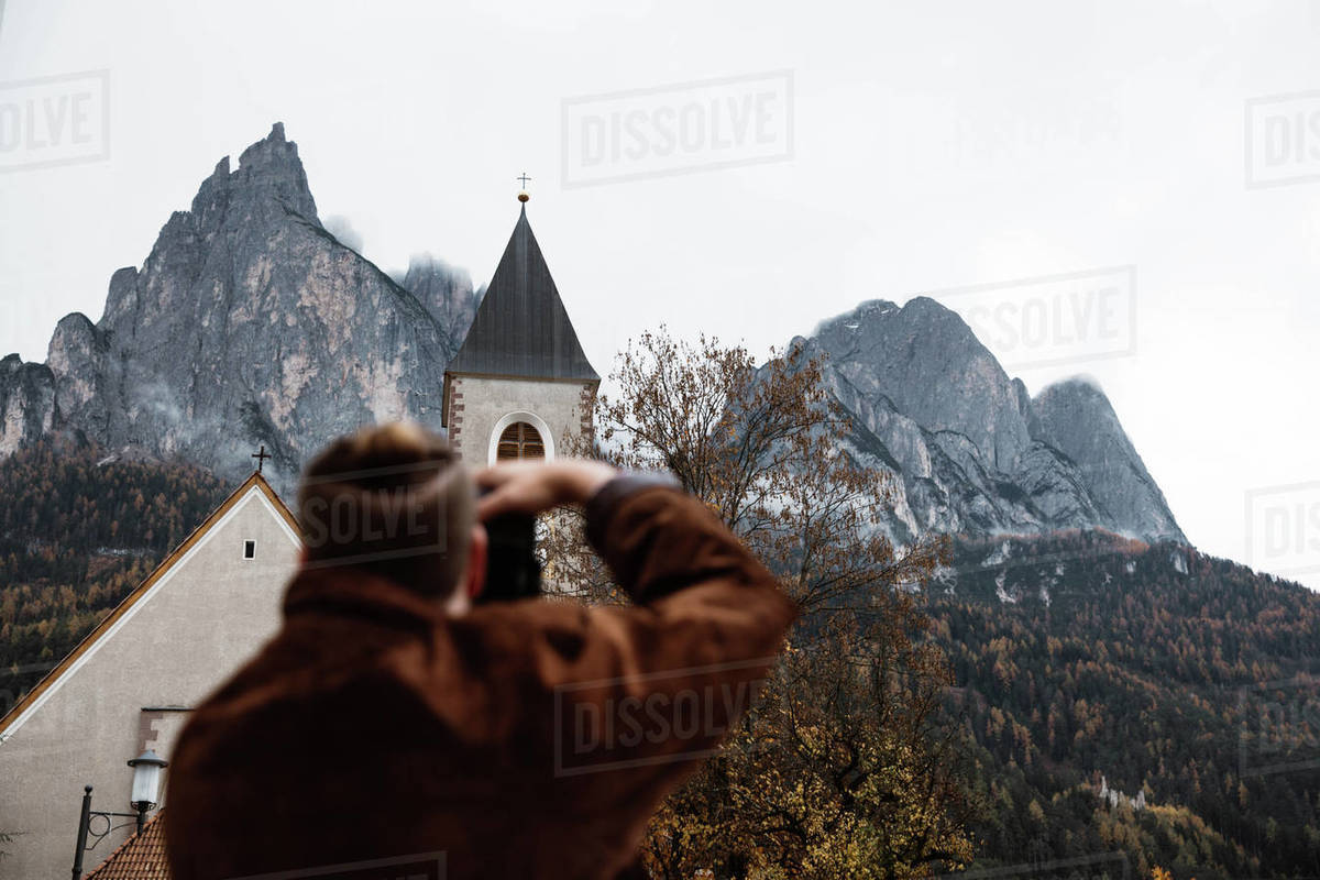 Back view of faceless male tourist in casual brown jacket taking photo ...