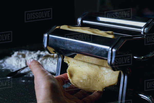 Crop person rolling dough through pasta machine while preparing fresh ...