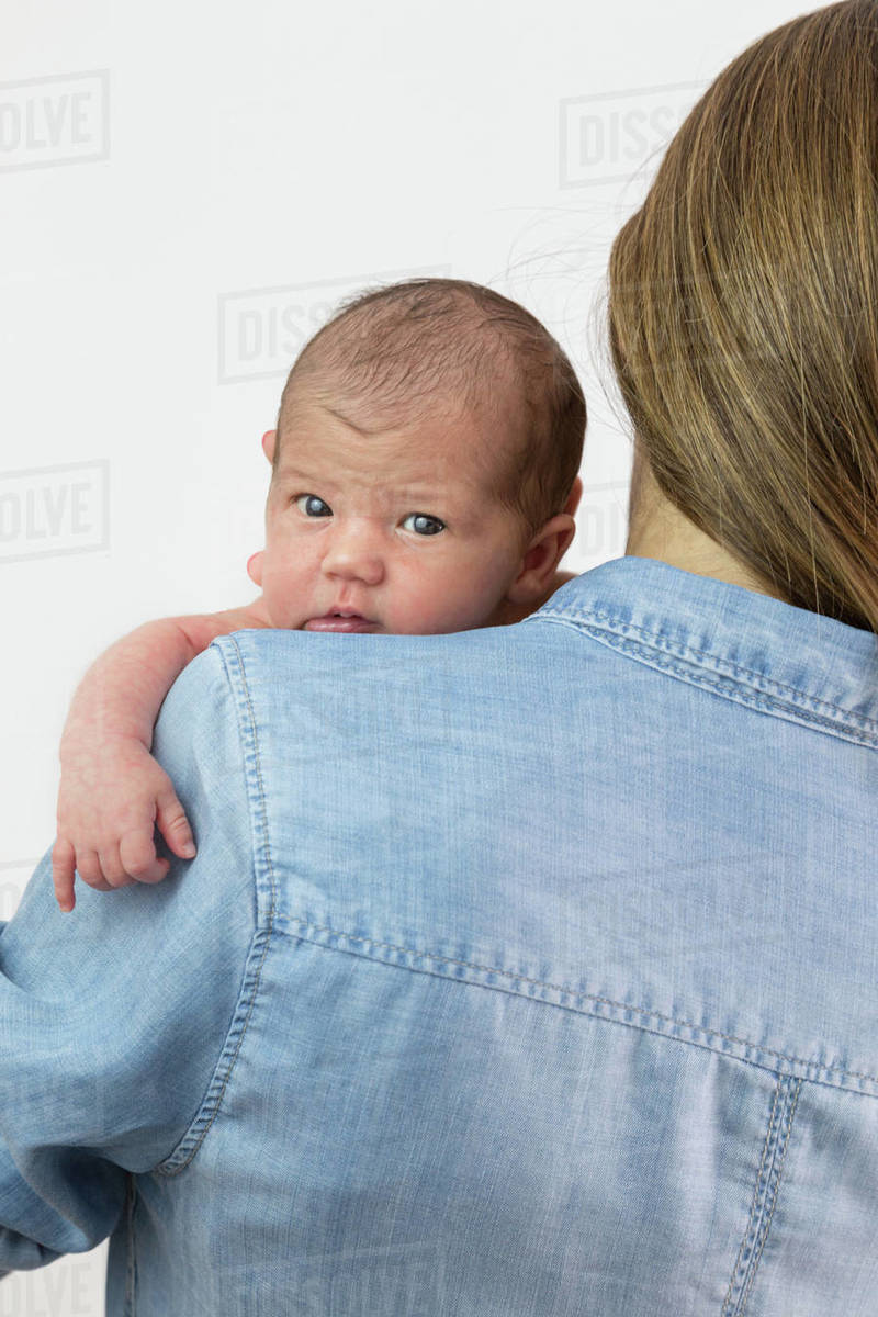 Back view of faceless female in denim blue shirt with tiny newborn with ...