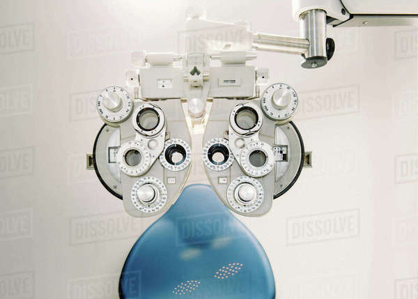 Modern vision test equipment and chair against white wall in optician ...