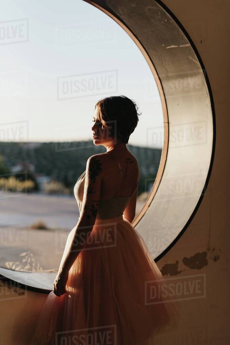 Back view of graceful lady in dance costume standing near round hole ...