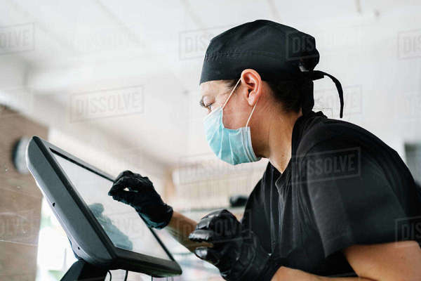 Side view serious female cashier wearing gloves and mask tapping on ...