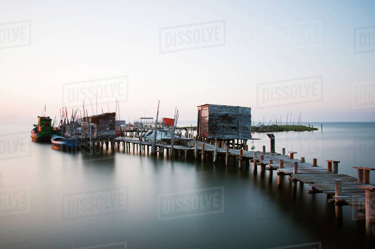 Wooden pier with thick sticks and shabby houseboat near moored modern ...