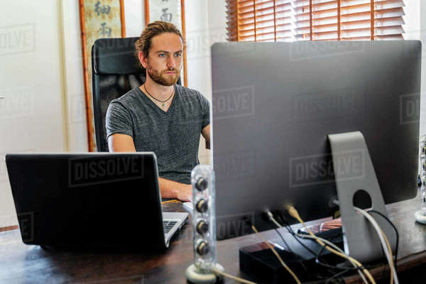 Handsome man working at desktop computer at home - Stock Photo - Dissolve