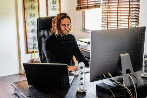 Handsome man working at desktop computer at home - Stock Photo - Dissolve