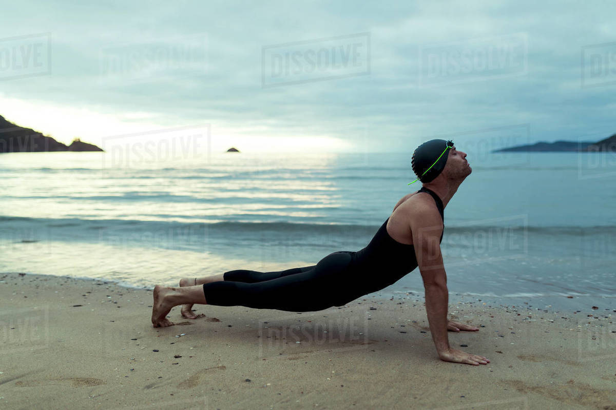 Side view of professional male swimmer in swimsuit and cap stretching ...