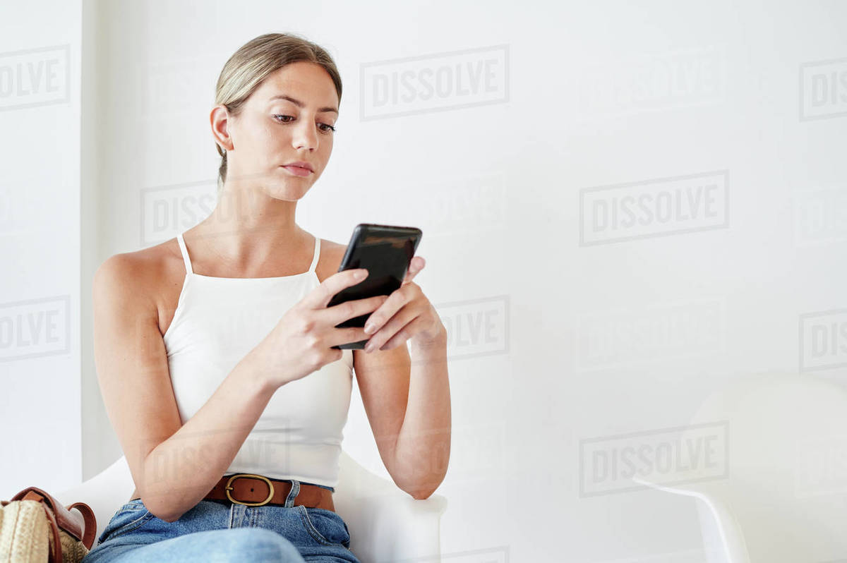 Female client sitting on chair and browsing on smartphone while waiting ...