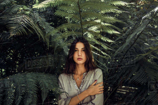 Tranquil female in summer outfit standing in shade of green leaves of ...
