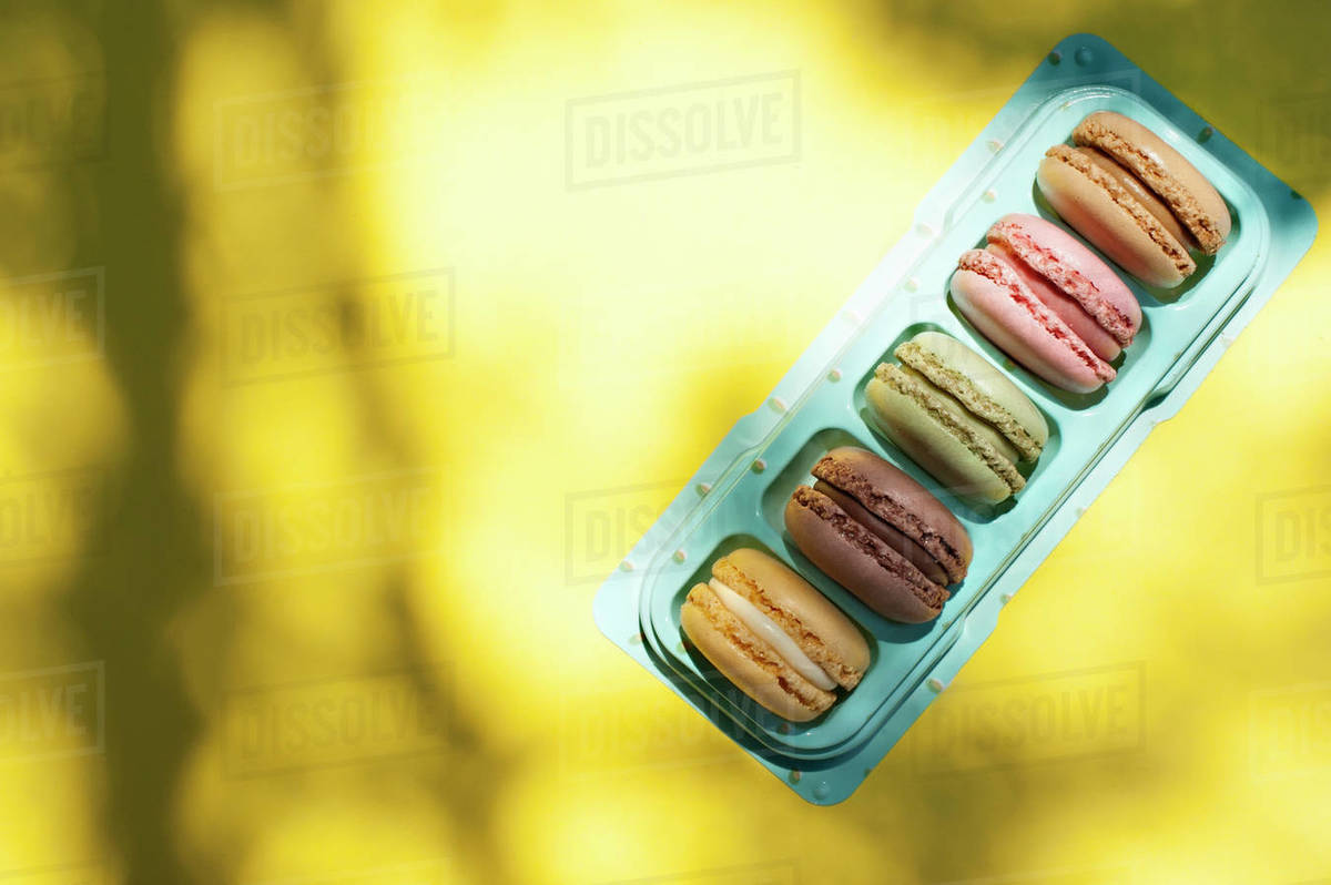Top view of sweet macarons in plastic container placed on yellow table ...