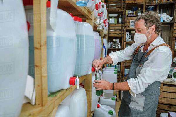 Side view of senior male seller in protective mask and apron filling ...