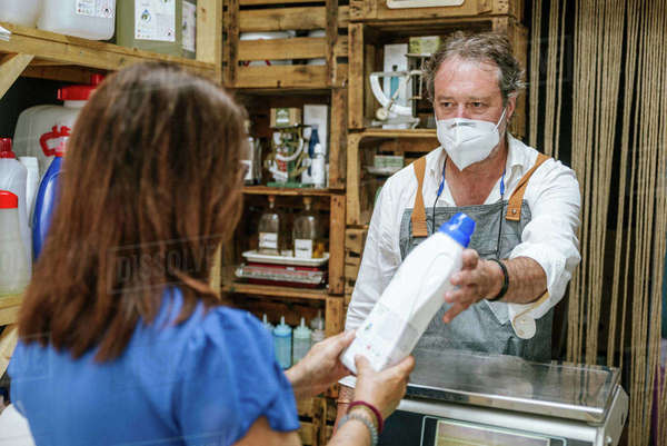 Senior male seller in protective mask standing at counter and sticking ...