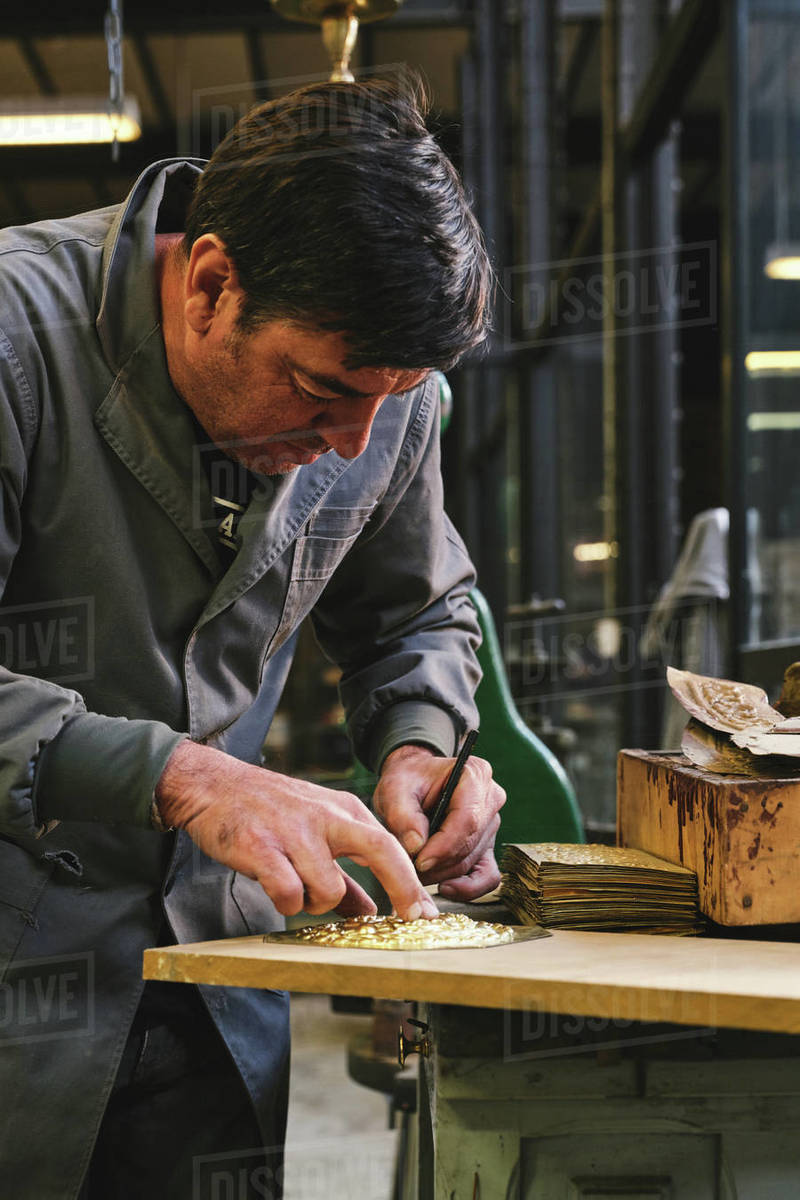 Concentrated middle aged ethnic goldsmith in uniform working with gold ...