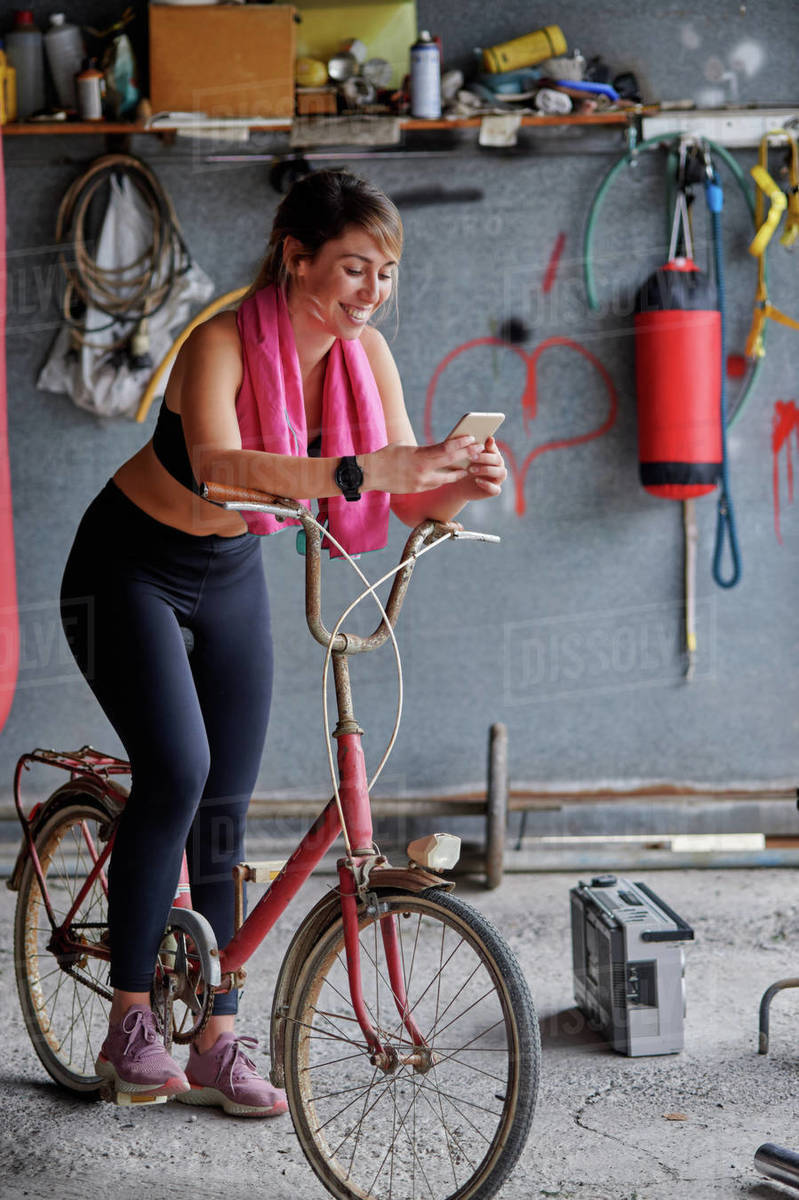 Full body smiling female bicyclist in sportswear sitting on bicycle and ...
