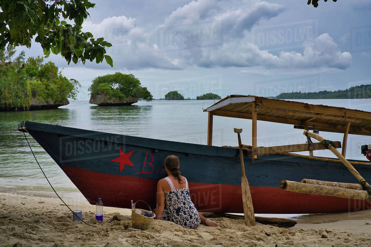 Back view of anonymous female in dress painting on wooden boat with red ...