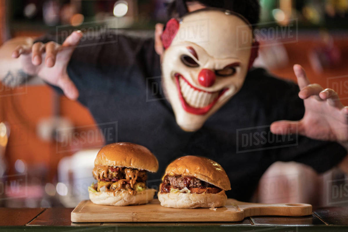 Male chef wearing scary clown mask standing at counter with delicious ...