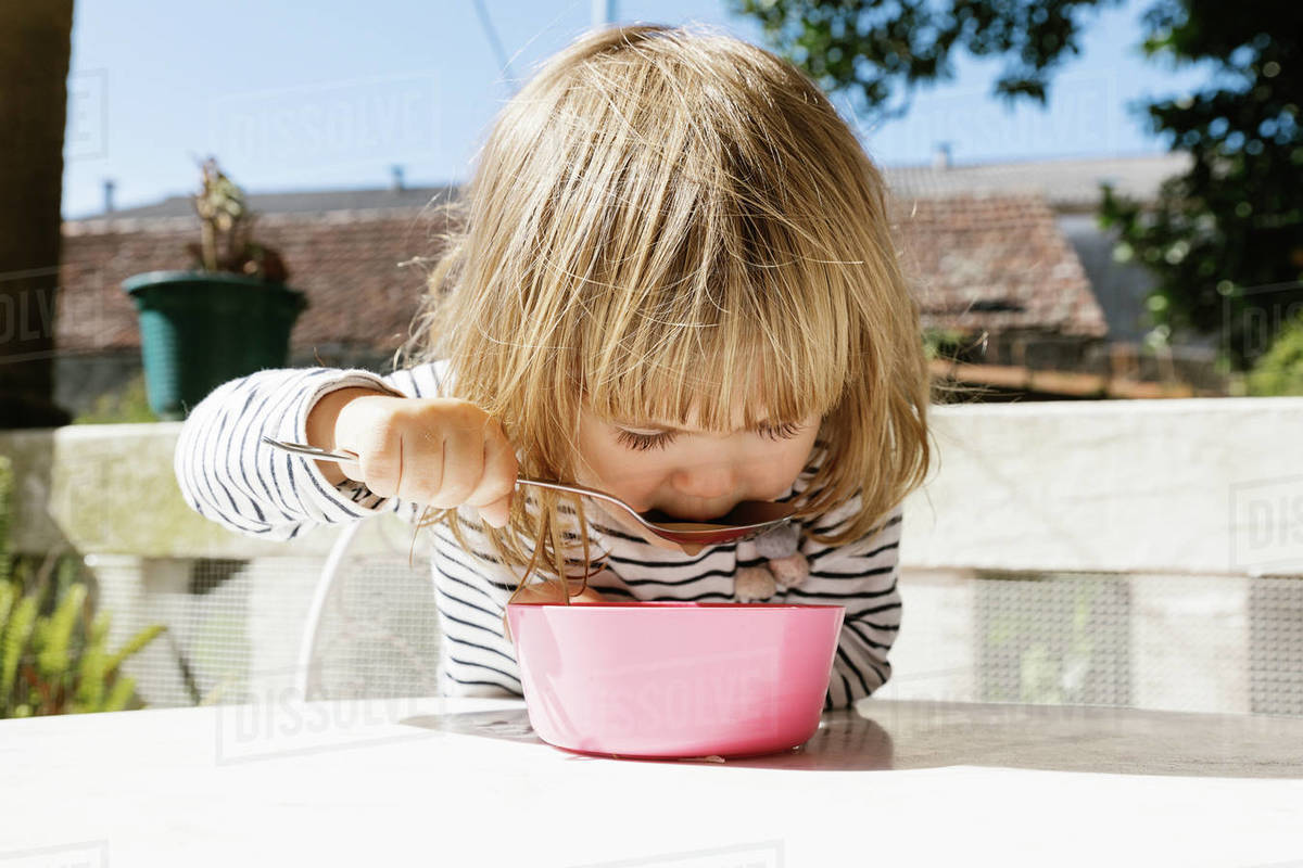 Adorable little child sitting at table eating from a pink bowl on ...