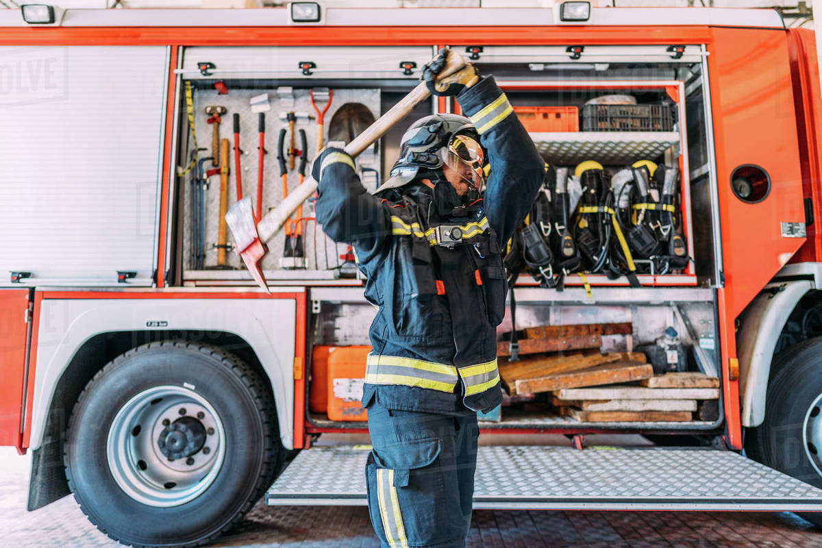 Side view of unrecognizable firefighter in uniform and hardhat carrying ...