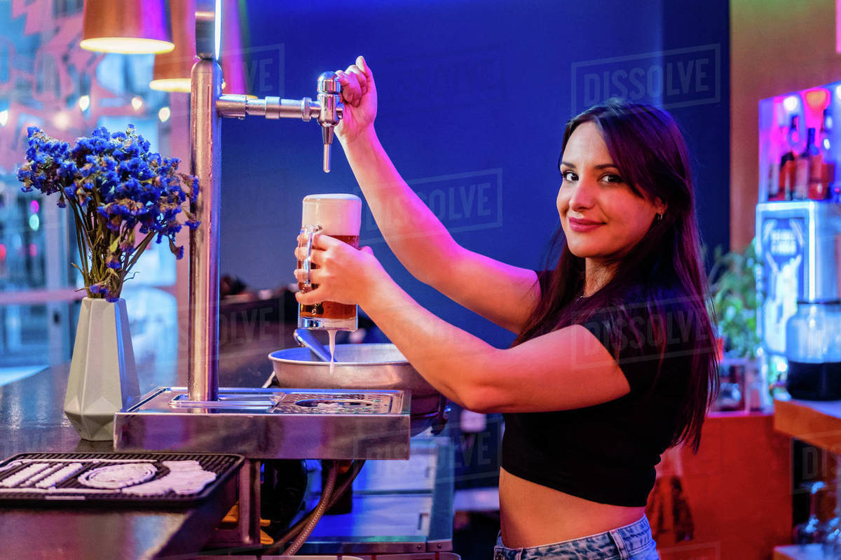 Side view of female bartender pouring alcoholic drink into glass while ...