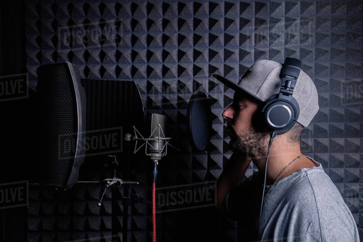 Side view of male singer in headphones and hat standing in acoustic ...