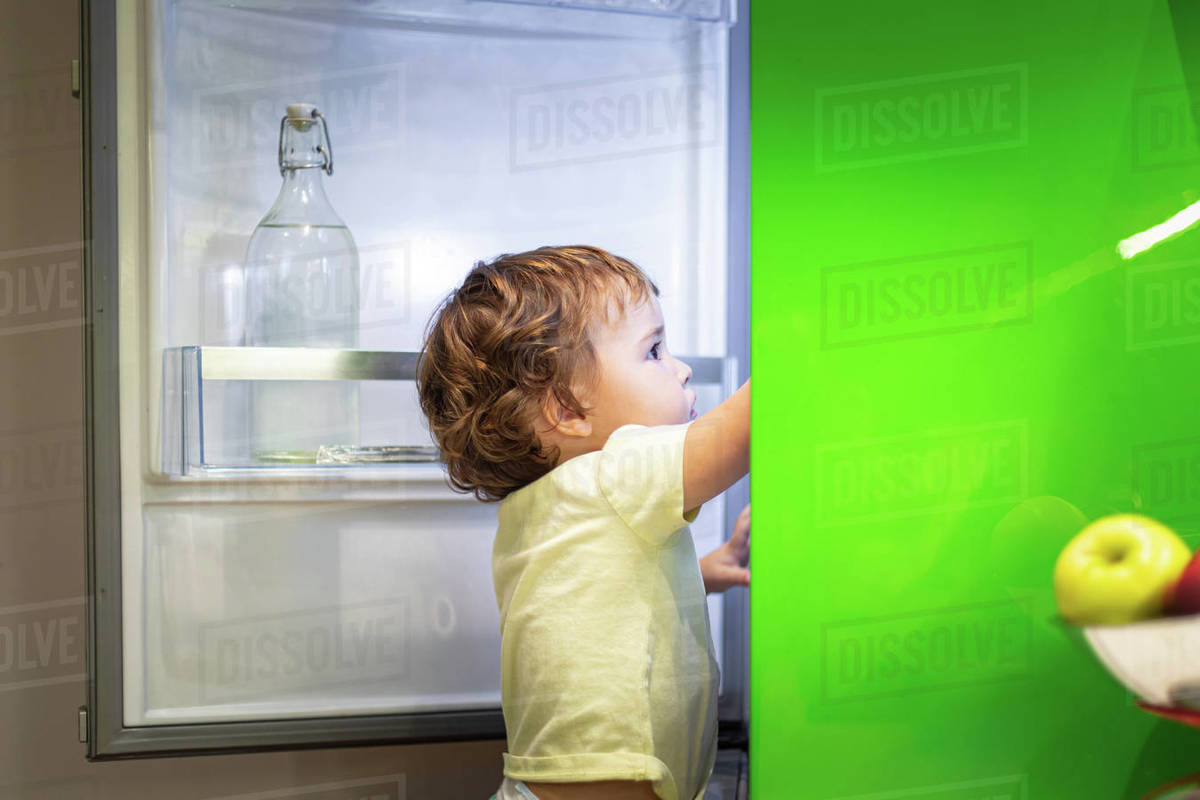 Side view of cute little child standing on stool and taking food from ...