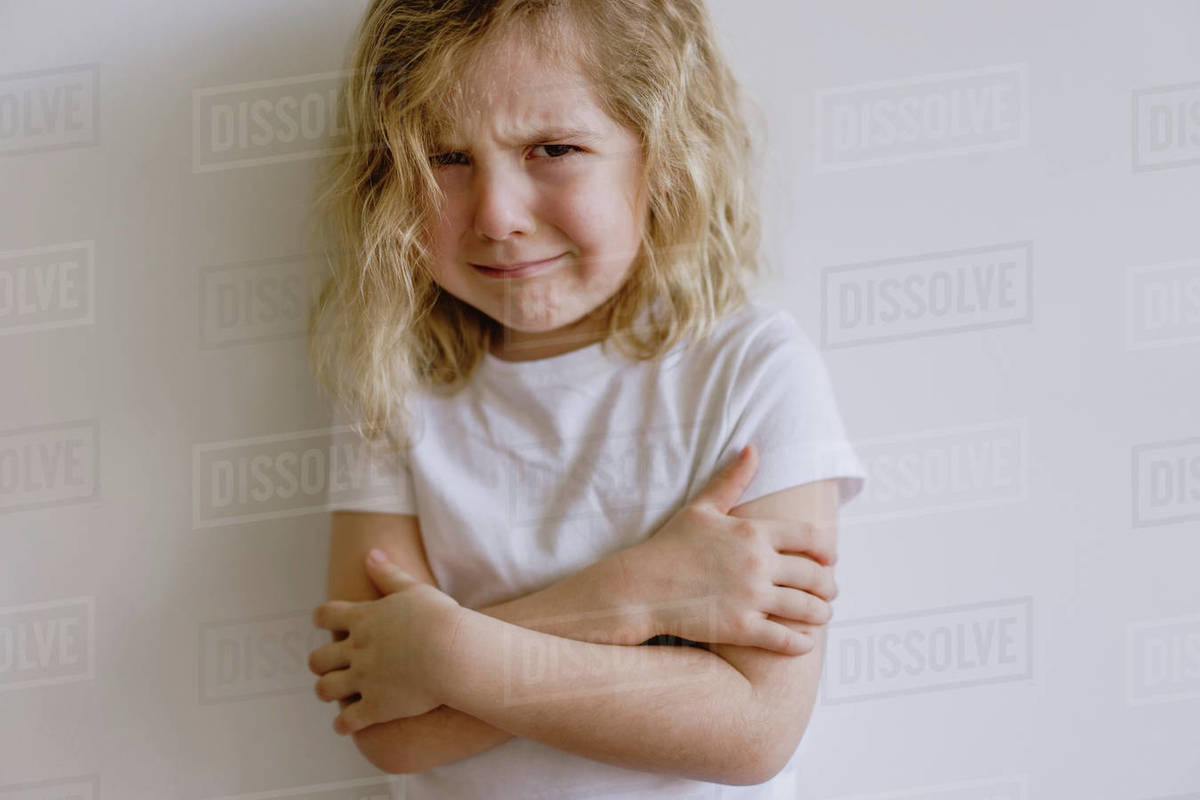 Naughty kid with wavy hair in casual clothing standing with folded arms ...