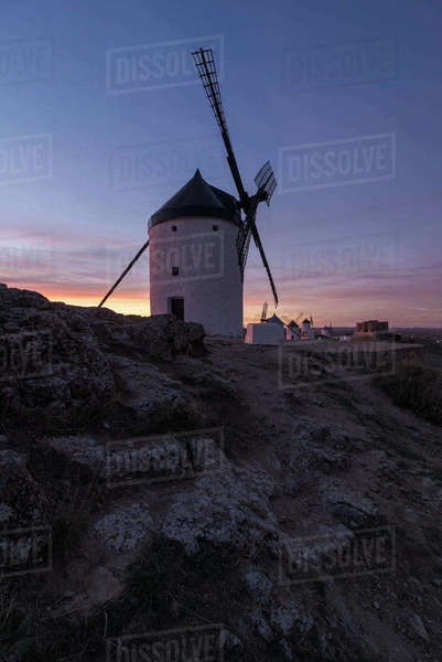 Aged windmill located on rocky cliff near medieval castle against ...