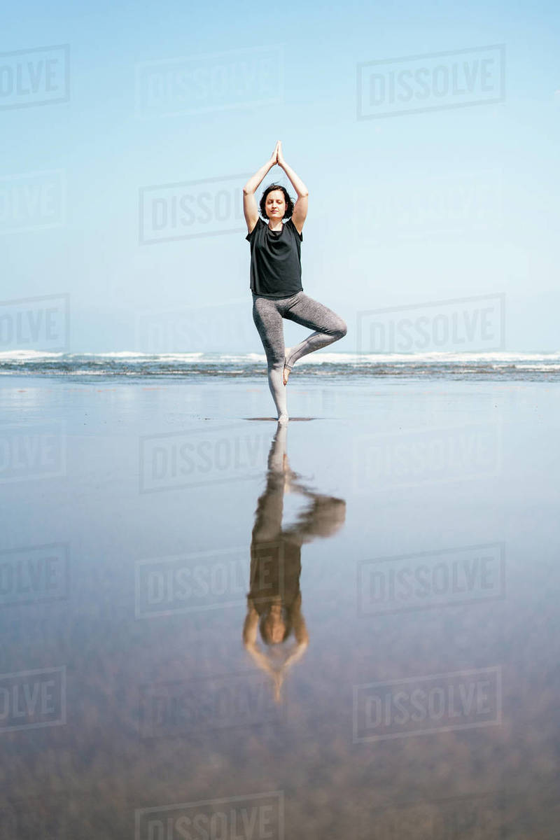 Full body young female in sportswear standing in Tree pose with arms up ...