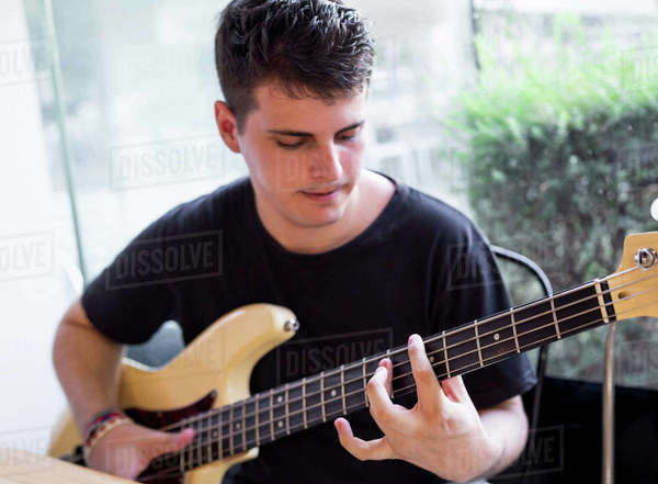 Focused young male musician sitting near window and performing music on ...