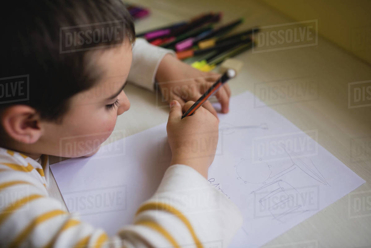 Side view of crop cute kid sitting at wooden table and drawing with ...