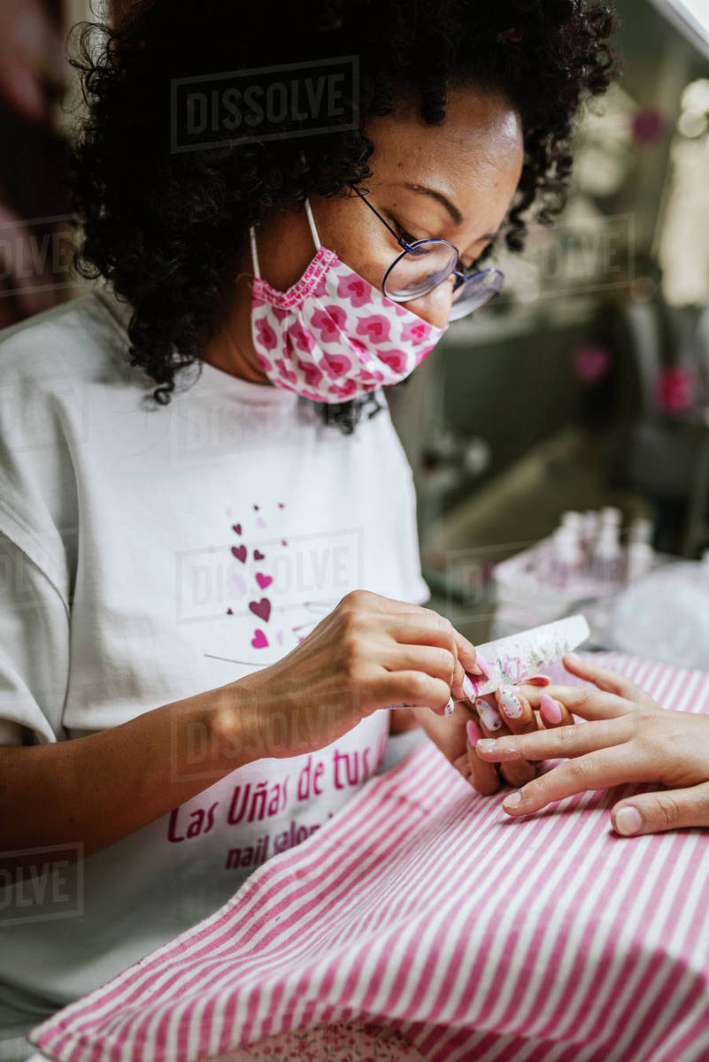 Side view of concentrated African American nail artist using file and ...