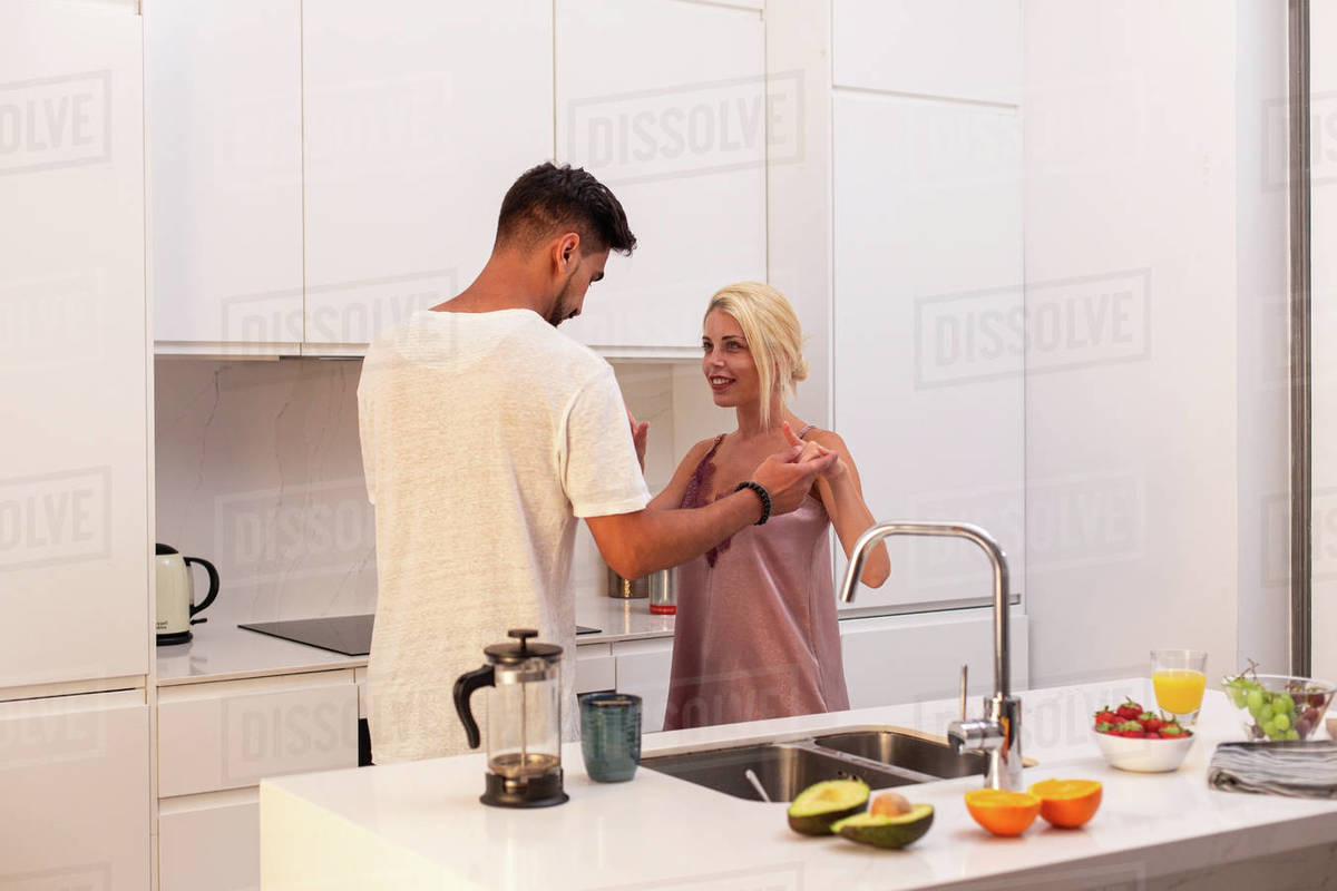 Side view of smiling couple cuddling in modern kitchen during breakfast ...