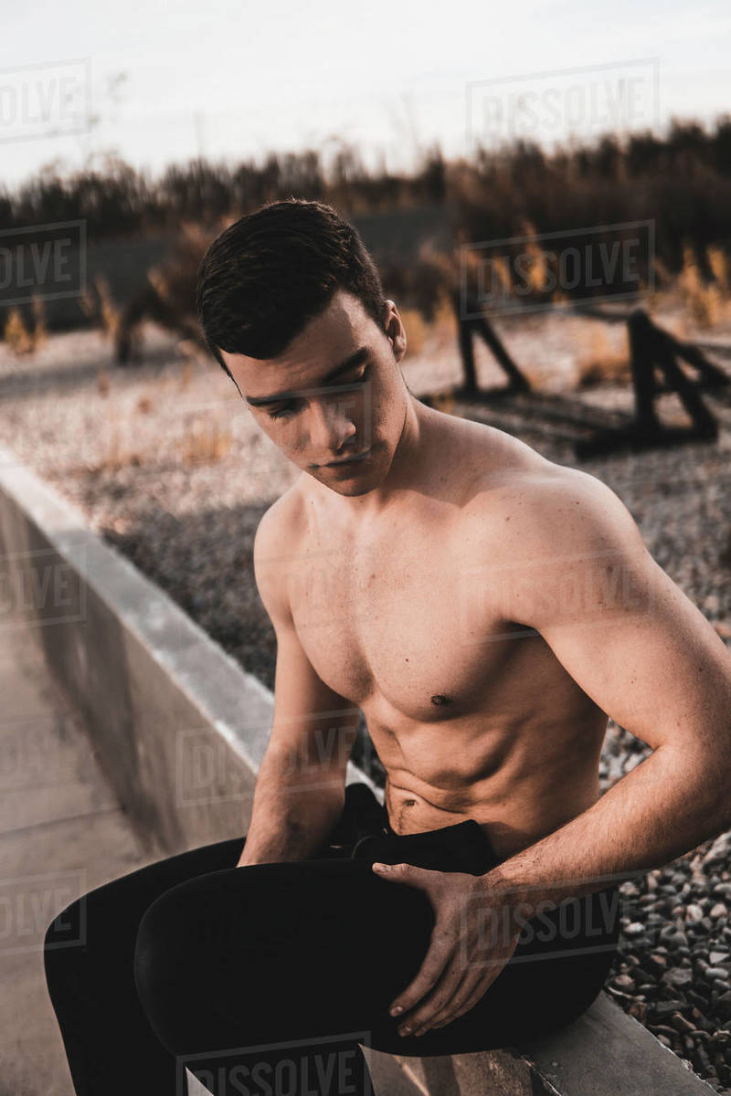 Side view of muscular shirtless guy looking at camera while leaning on ...