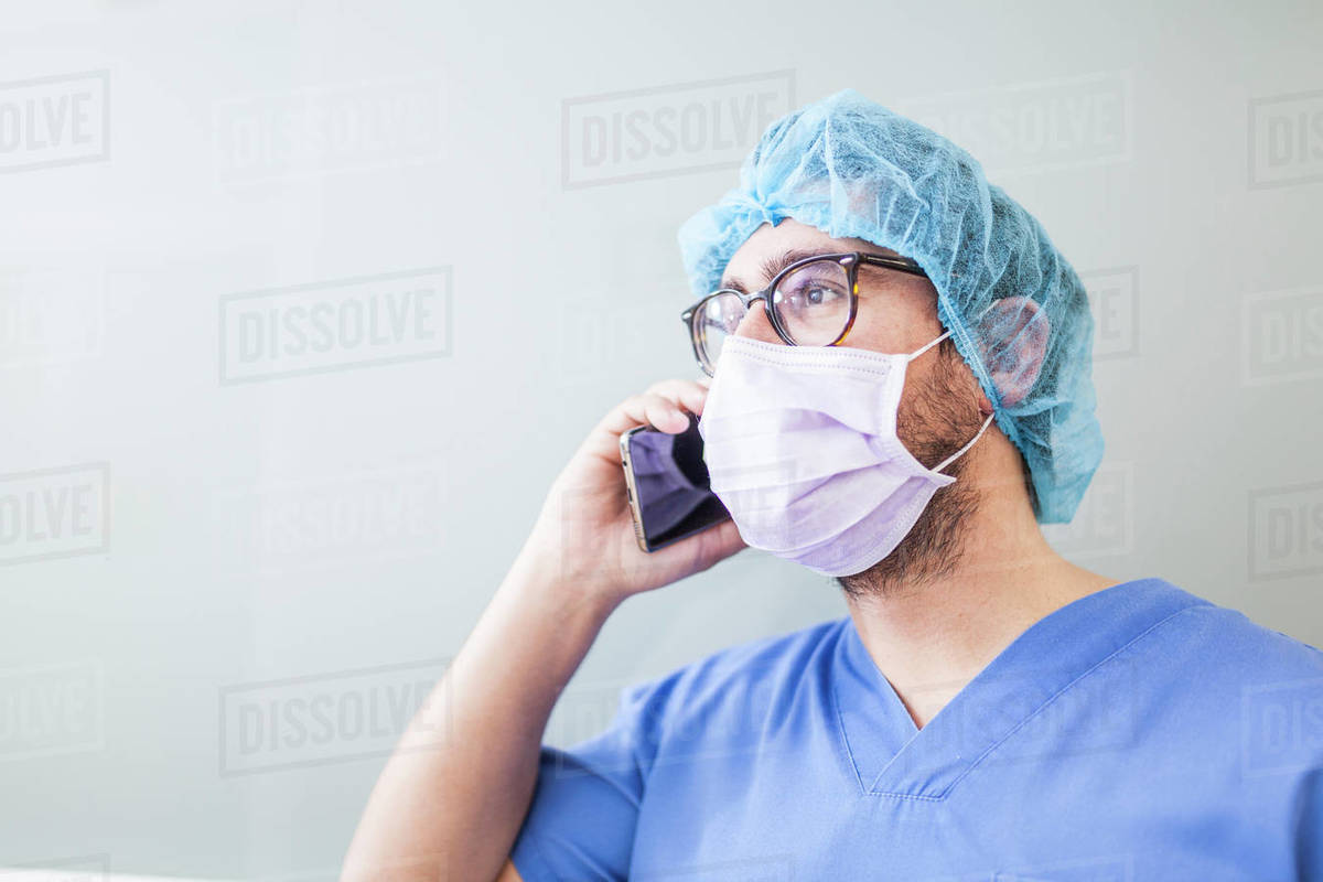 Male surgeon leaning on corridor wall while talking with his smart ...