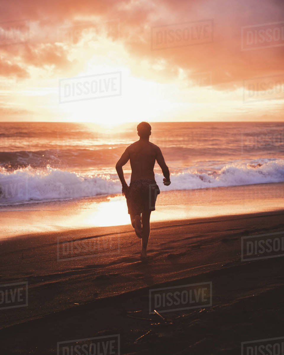 Back view of man running on coastline against powerful ocean waves and ...