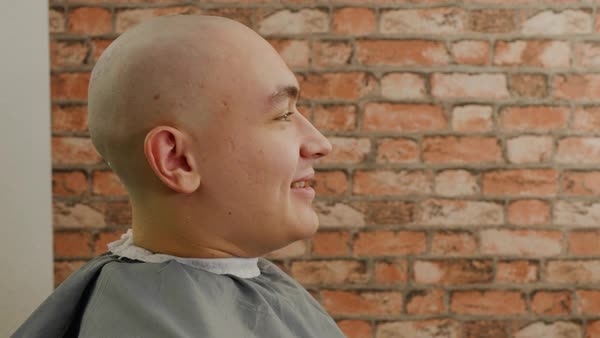Bald man with shaved head sitting in barber chair in male salon ...
