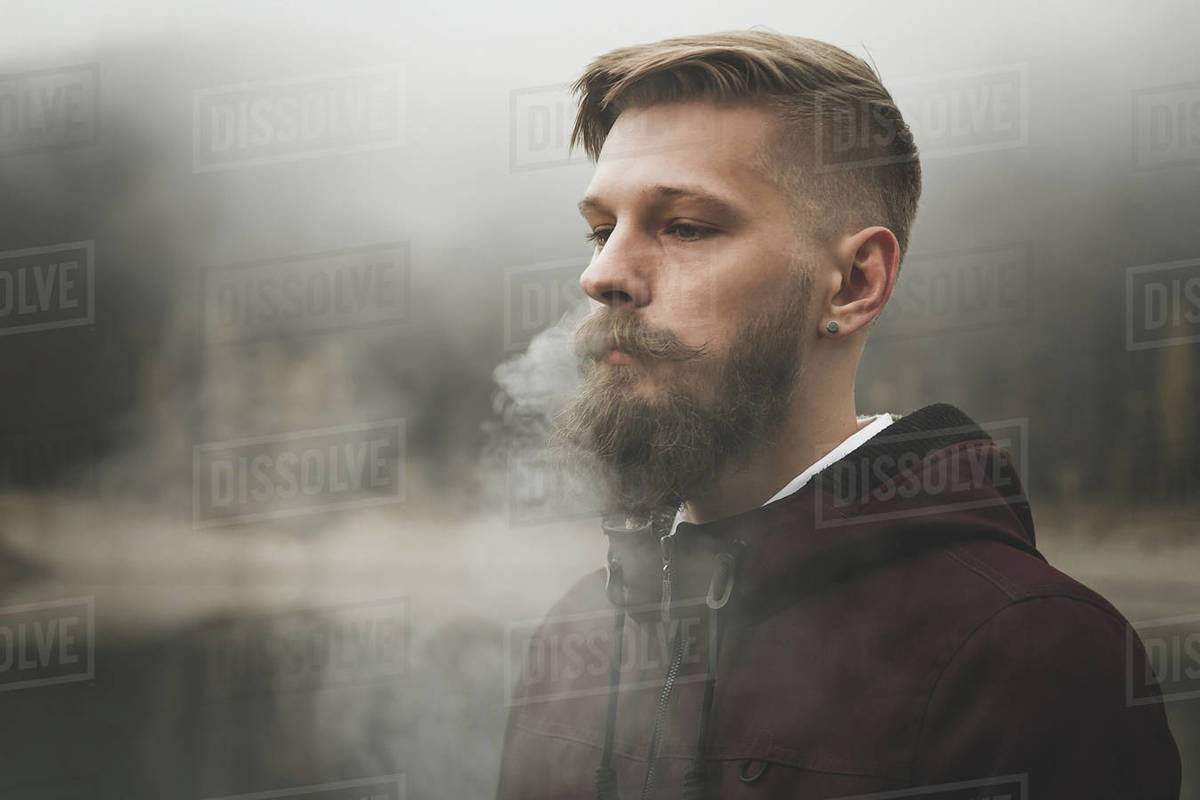 Handsome bearded man smoking cigarette Blows out steam through the ...