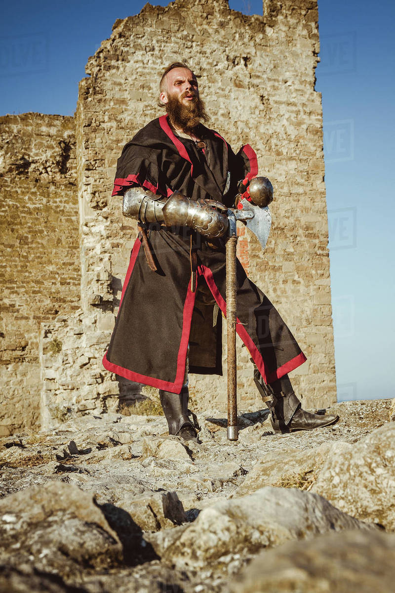 A man with a beard in a knight's costume with an ax looks into the ...