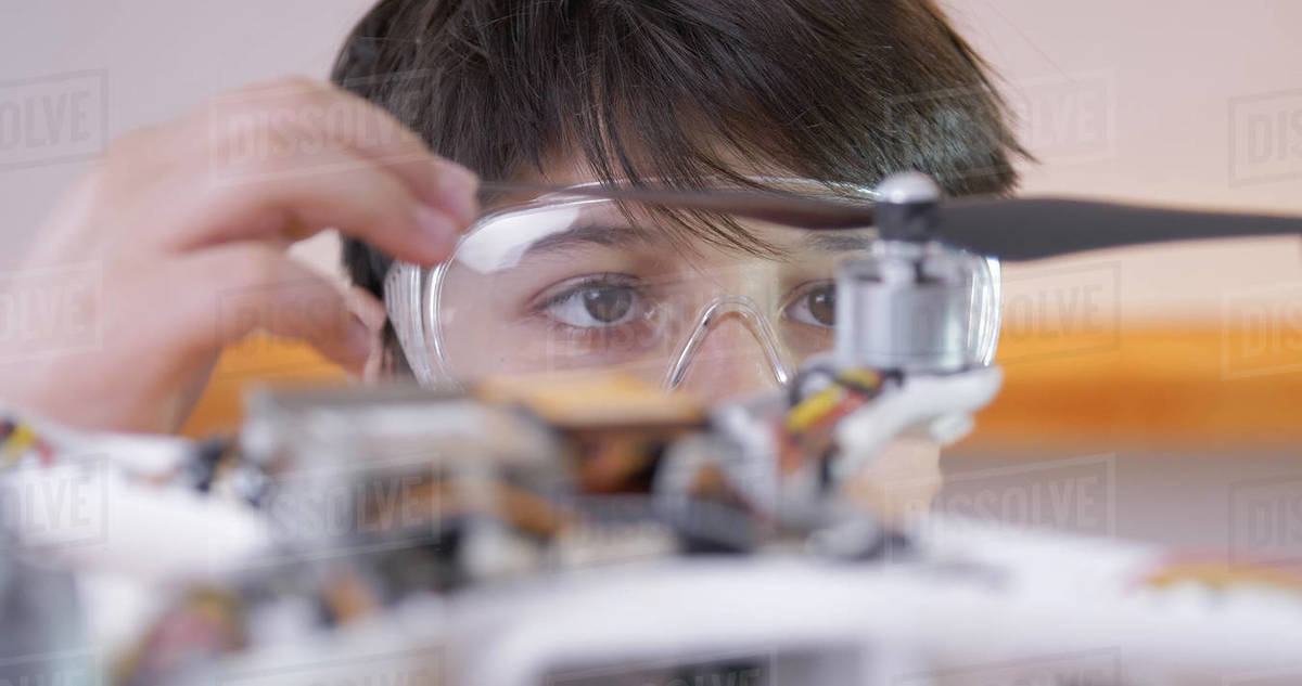 A boy wearing goggles installs a propeller on a disassembled drone ...
