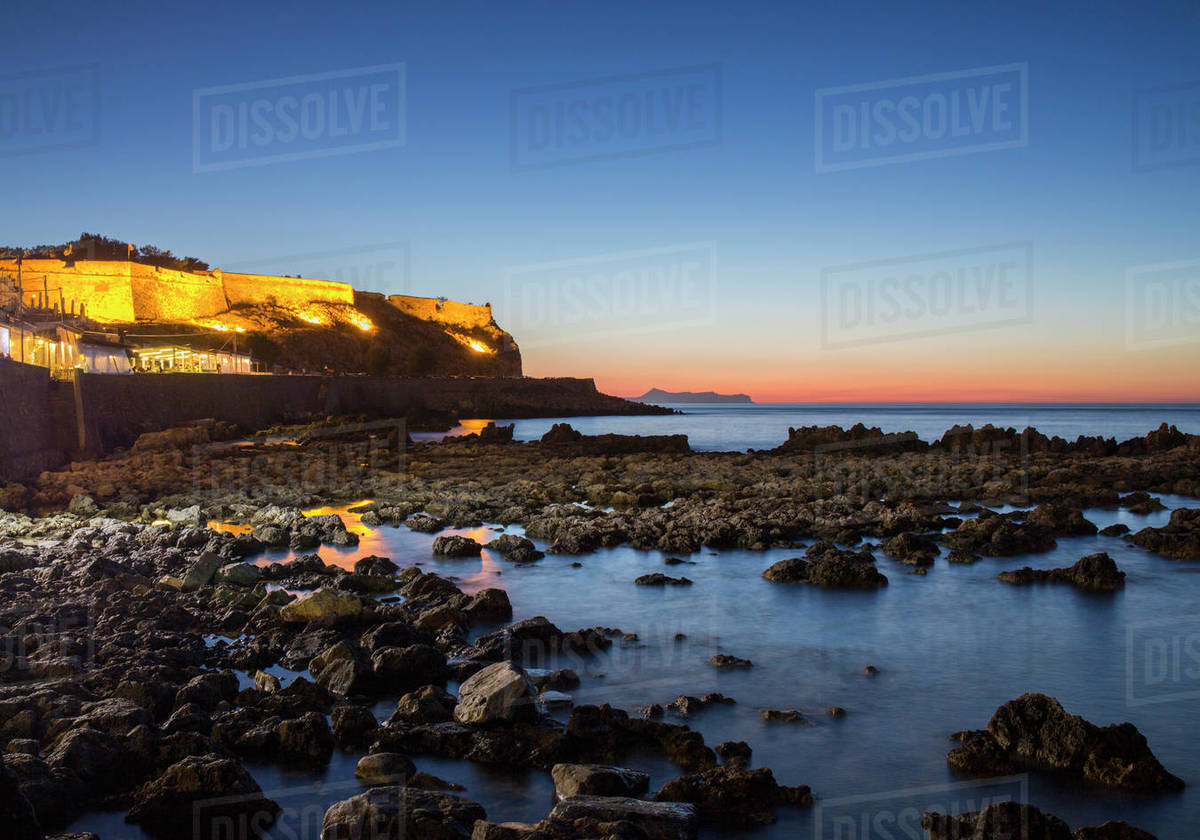 View from rocky shore to the illuminated Fortezza and distant Akrotiri ...